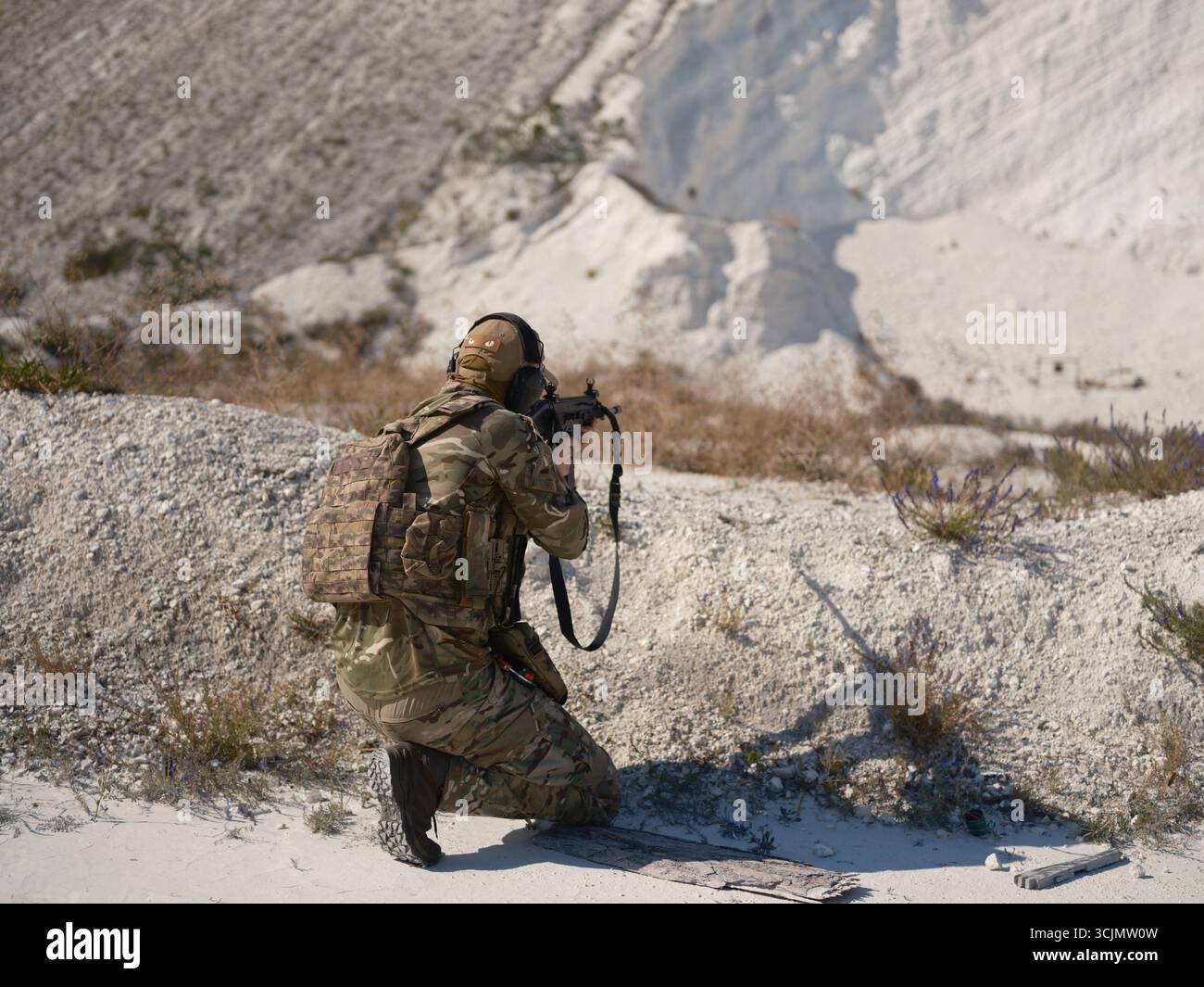 Ukrainian soldier in tactical vest kneels and aims rifle, ready for ...