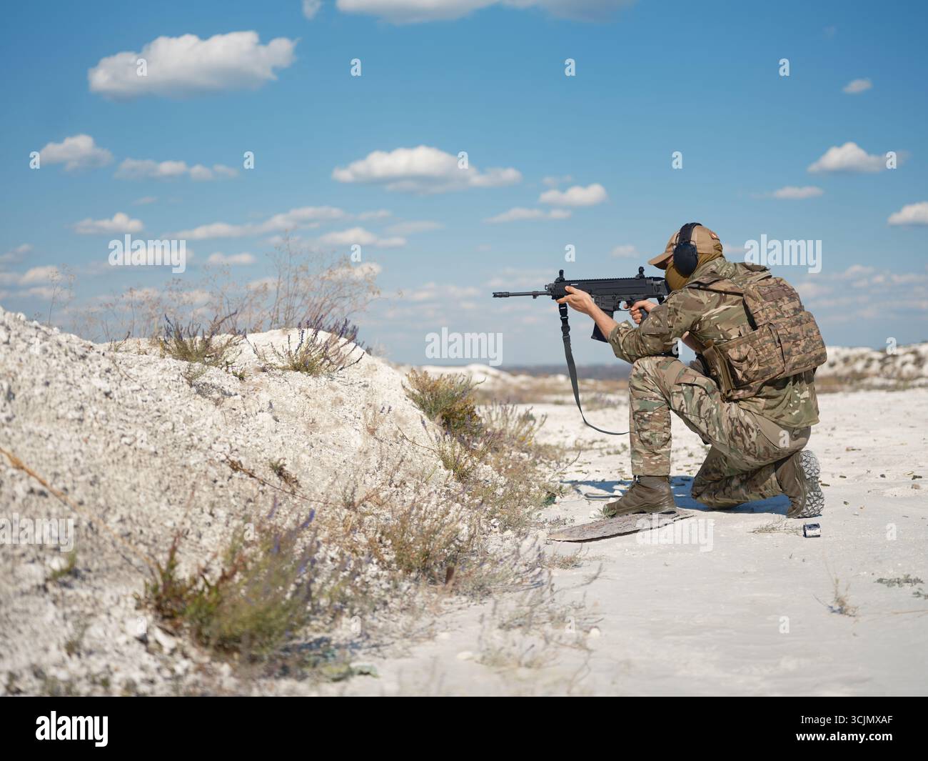 Ukrainian soldier in tactical vest kneels and aims rifle, ready for ...
