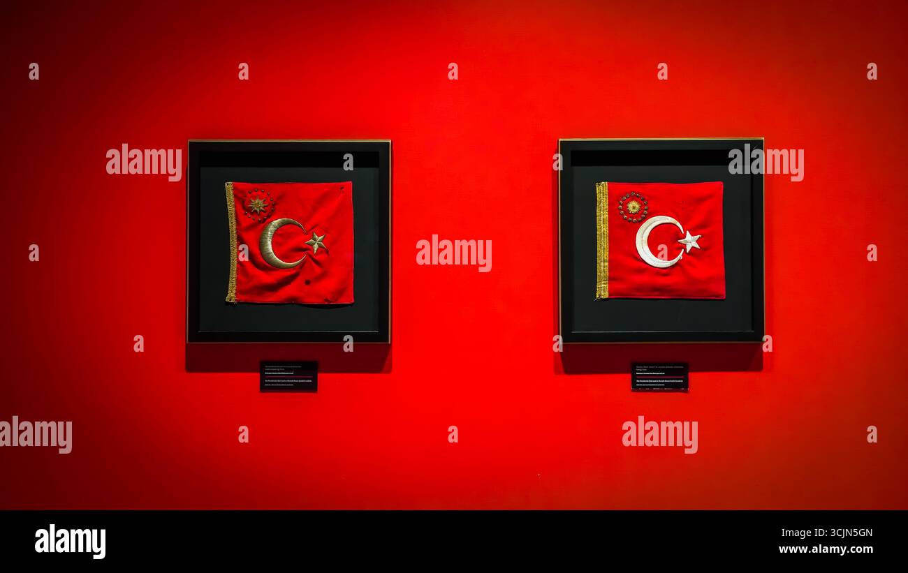 Ancient and antique Turkish flags are displayed in frames on a red wall ...