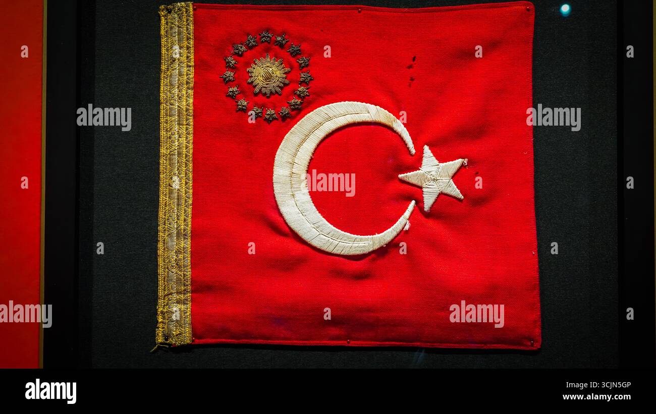 Ancient and antique Turkish flags are displayed in frames on a red wall ...