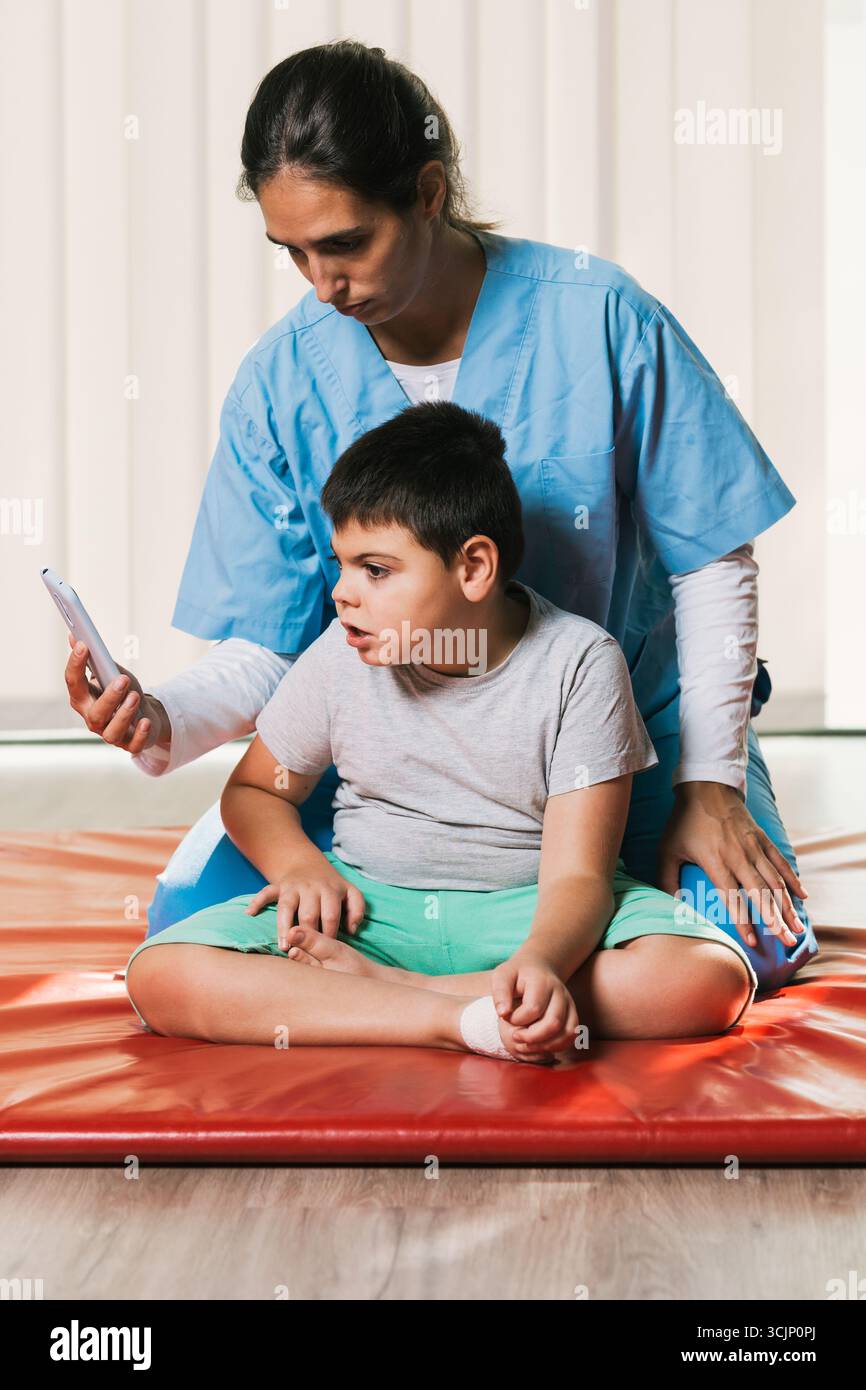 Physiotherapist showing smartphone to child with cerebral palsy during ...