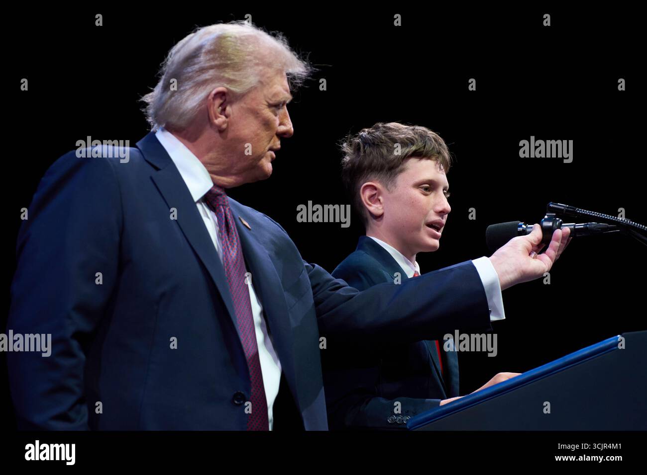 President Donald Trump adjusts the microphone for Shea Encinas, 12, of ...