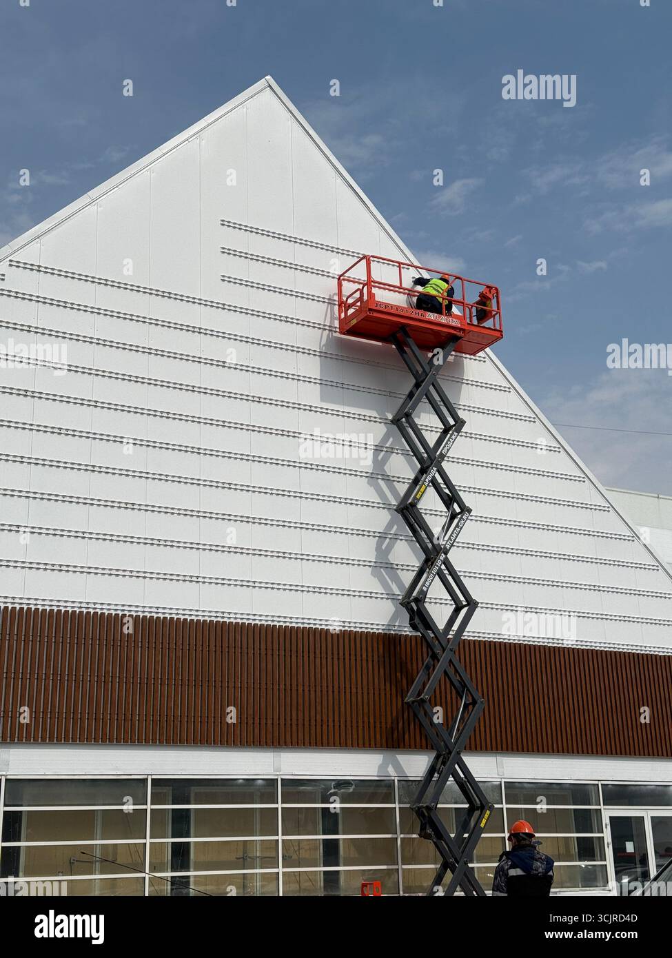 Workers install a commercial sign on a facade while standing on the ...