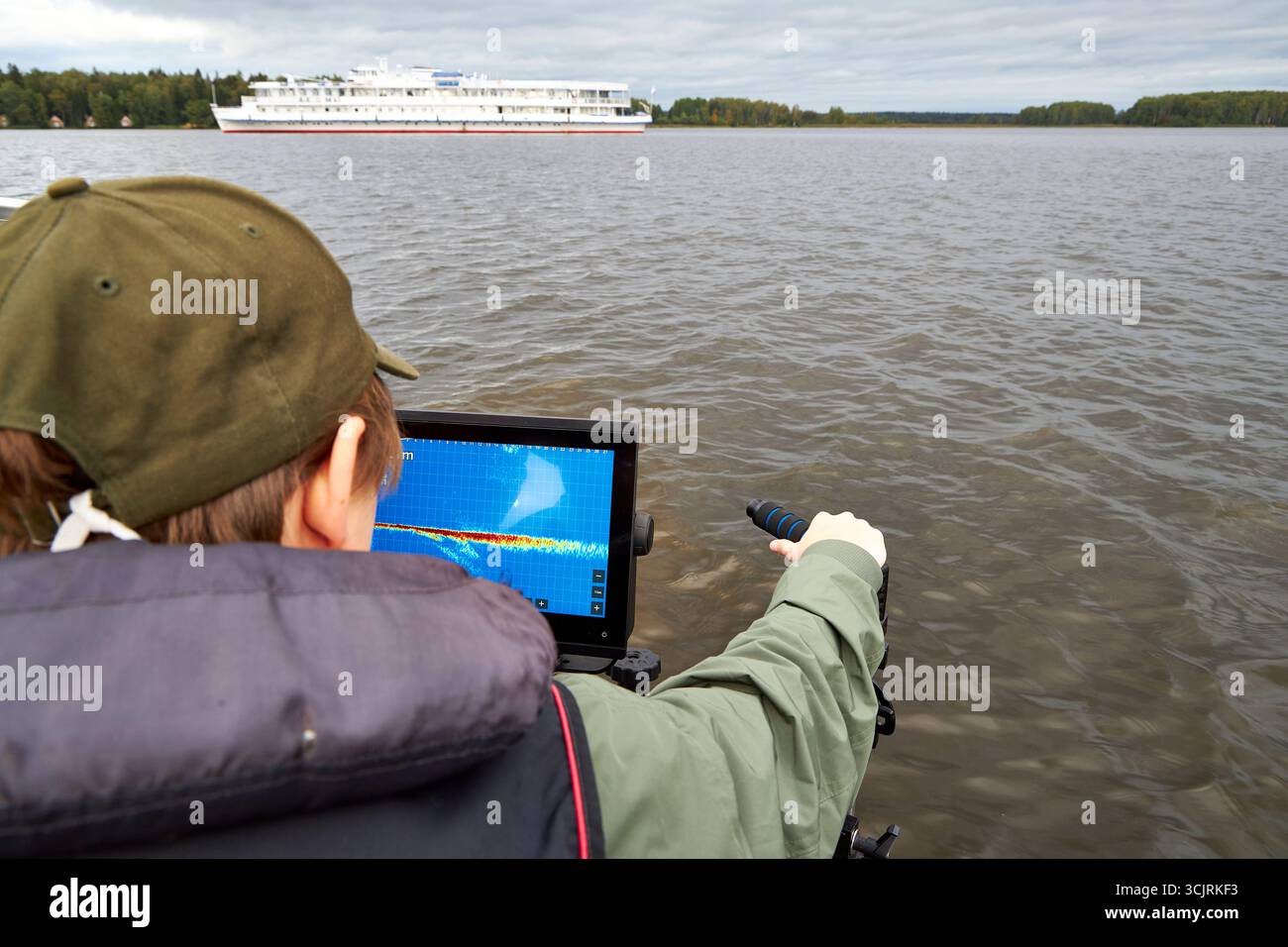 Fisherman steering boat while looking at fishfinder screen on a lake ...