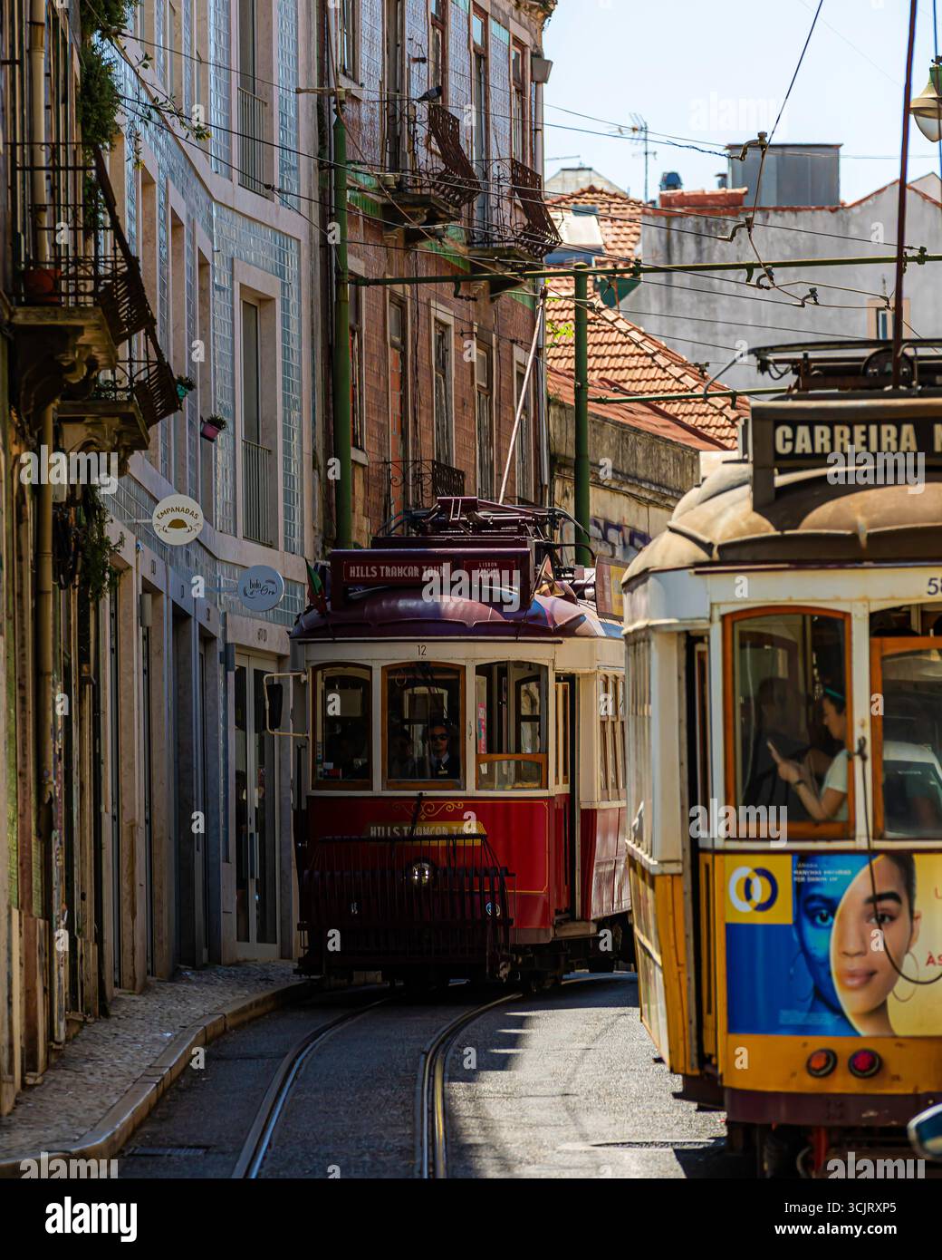 Lisbon, Portugal - Red and white trolley is traveling down a street. A ...