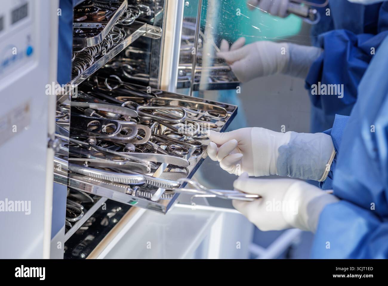 Technician in blue scrubs organizes clean metal tools on racks inside a ...