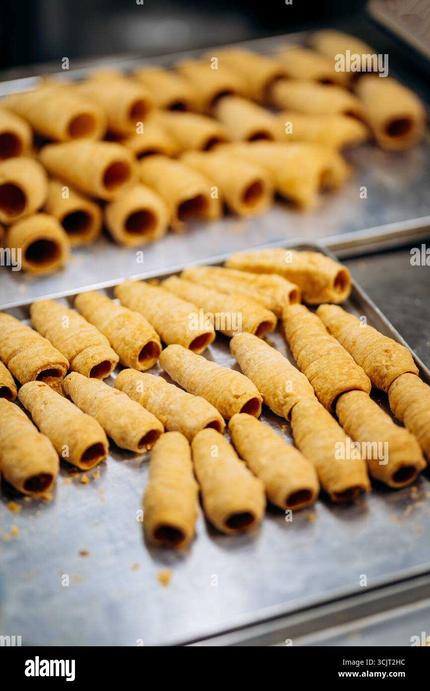 Unbaked puff pastry tubes on tray ready for cream filling in bakery ...