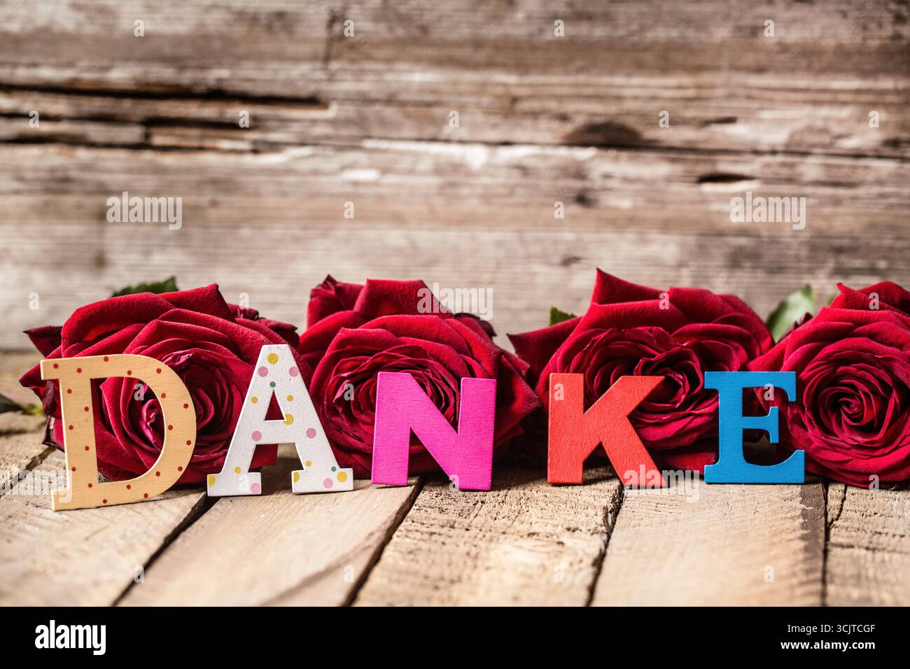 the German word Danke, thank you, in front of red roses and a wooden ...