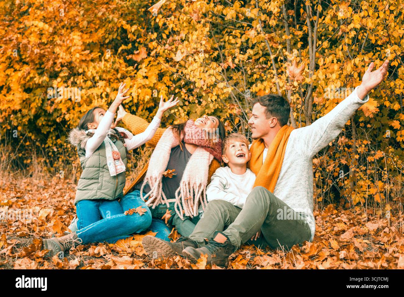 family with two children sitting boisterously laughing in the autumn ...