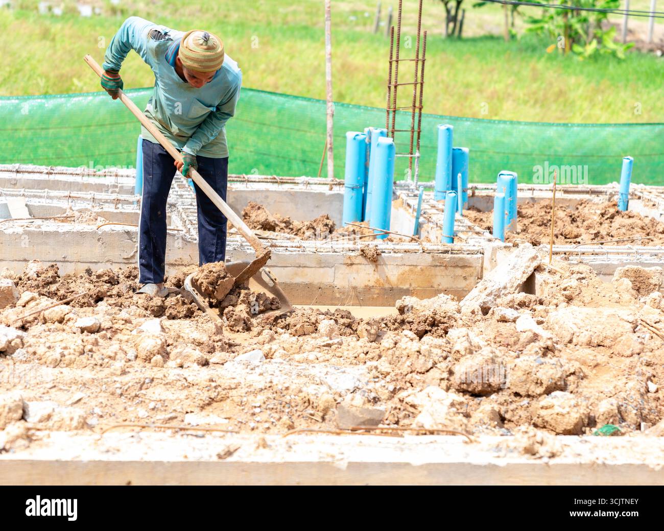 The worker is manually handling earth between concrete footing lines ...