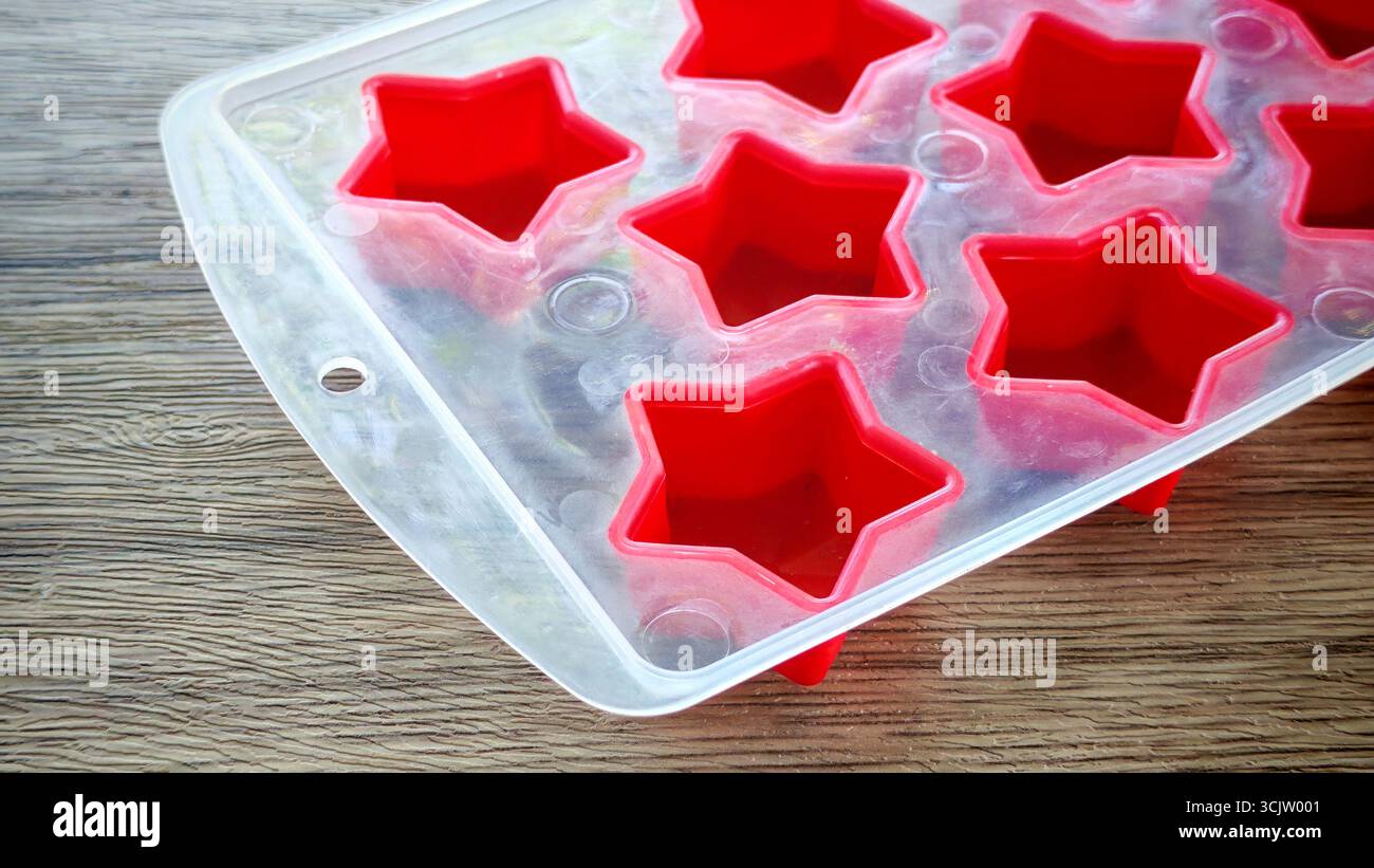 Empty red silicone star molds in a transparent tray on a wooden table ...