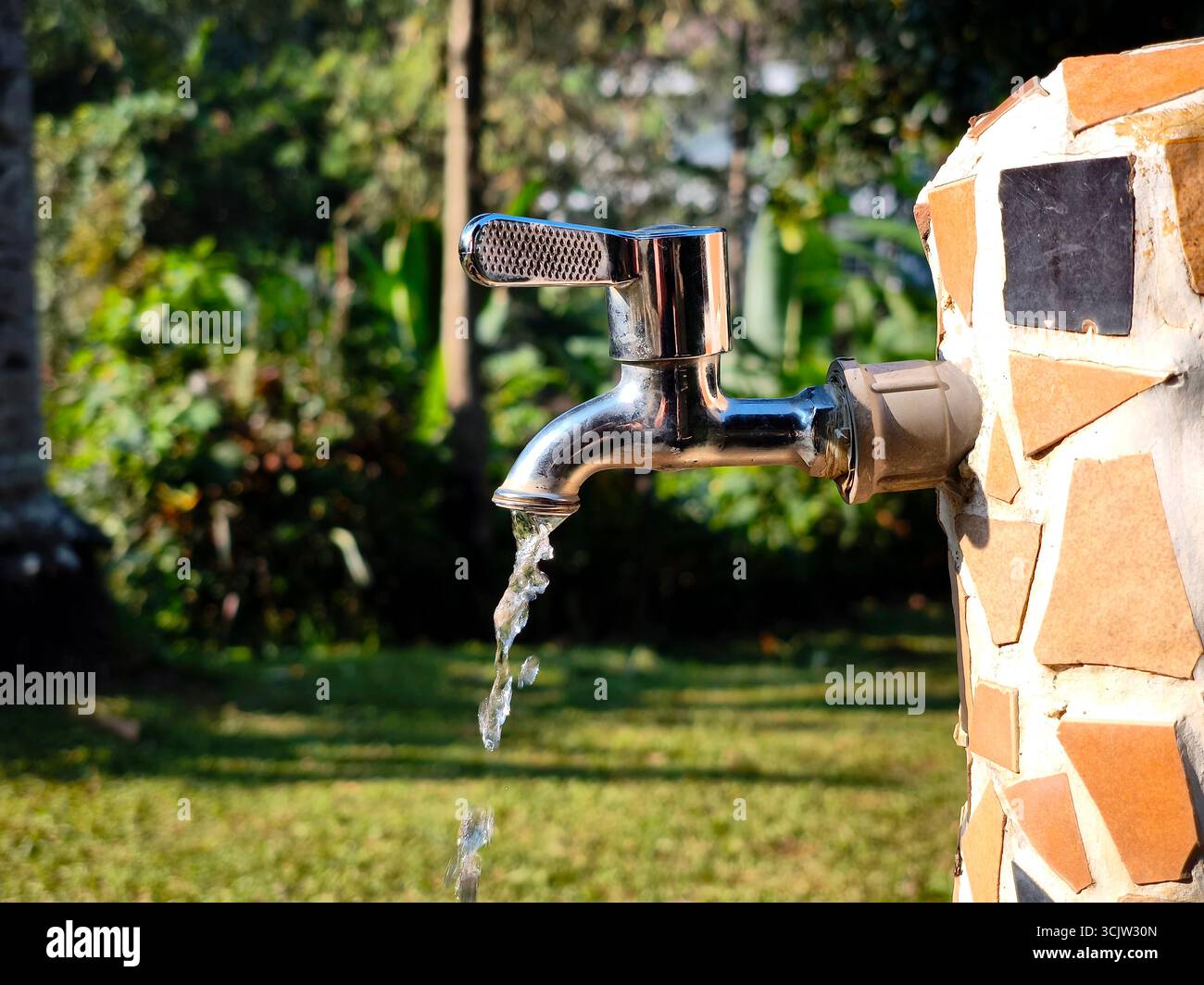 A close-up of a shiny metal water faucet mounted on a wall decorated ...