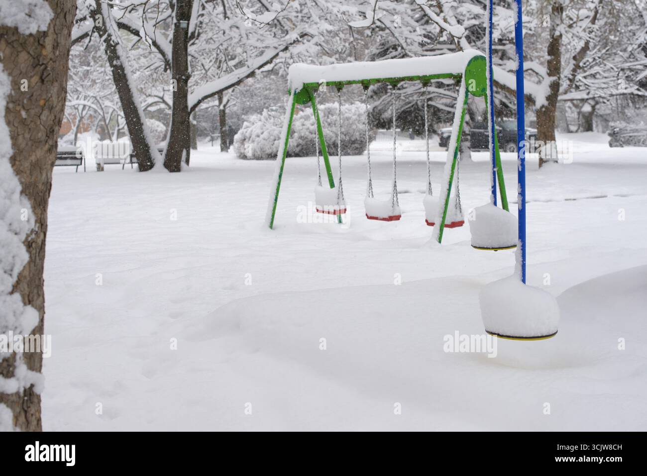 Snow-covered playground swings during heavy winter snowfall in an urban ...