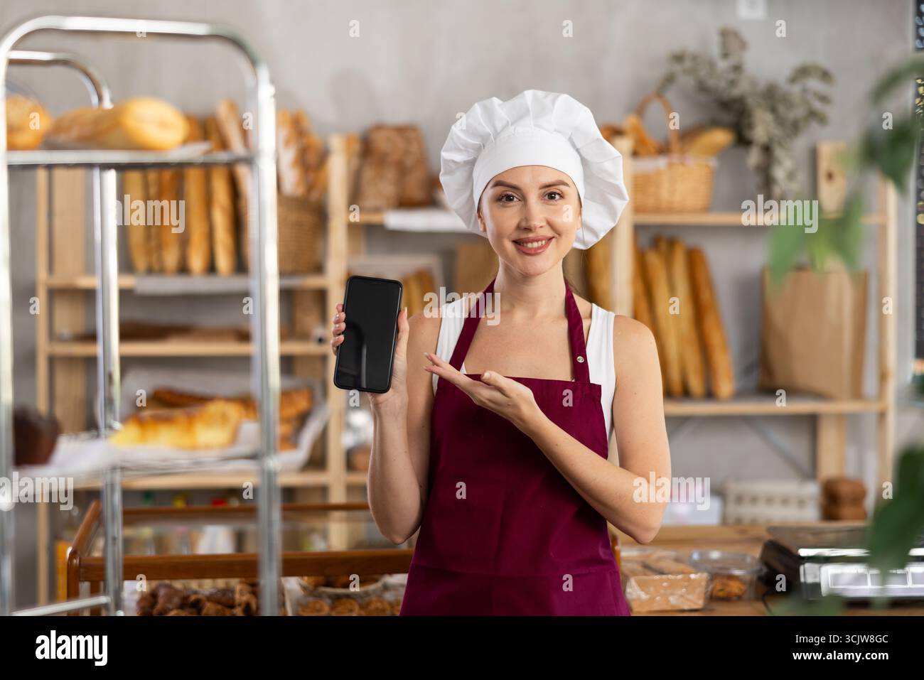 Portrait of female baker with mobile phone in hands in bakery interior ...