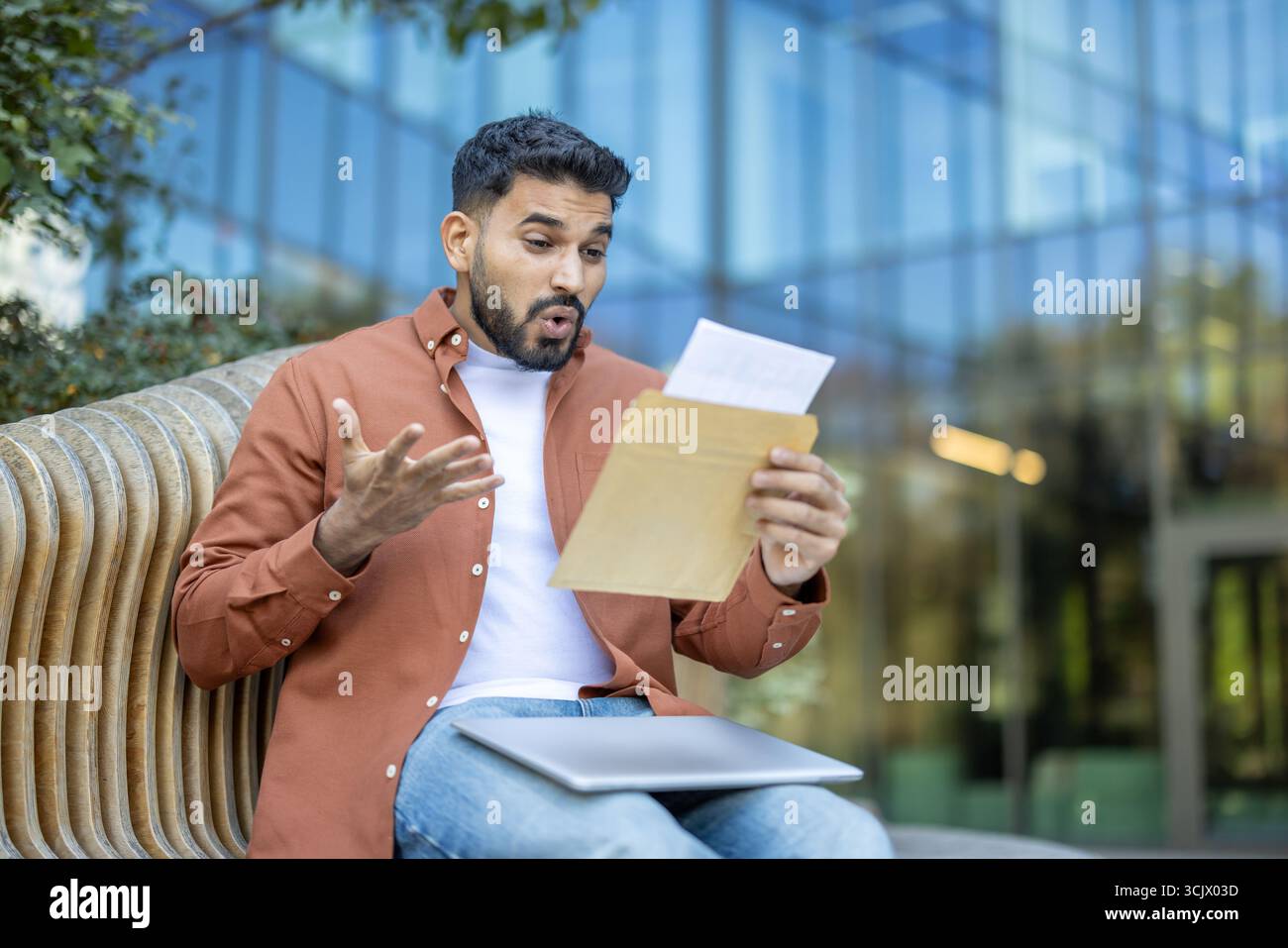Surprised businessman sitting on a bench outdoors, reacting with shock ...