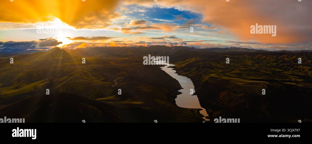 A winding lake flows through a valley of green hills and mountains in ...