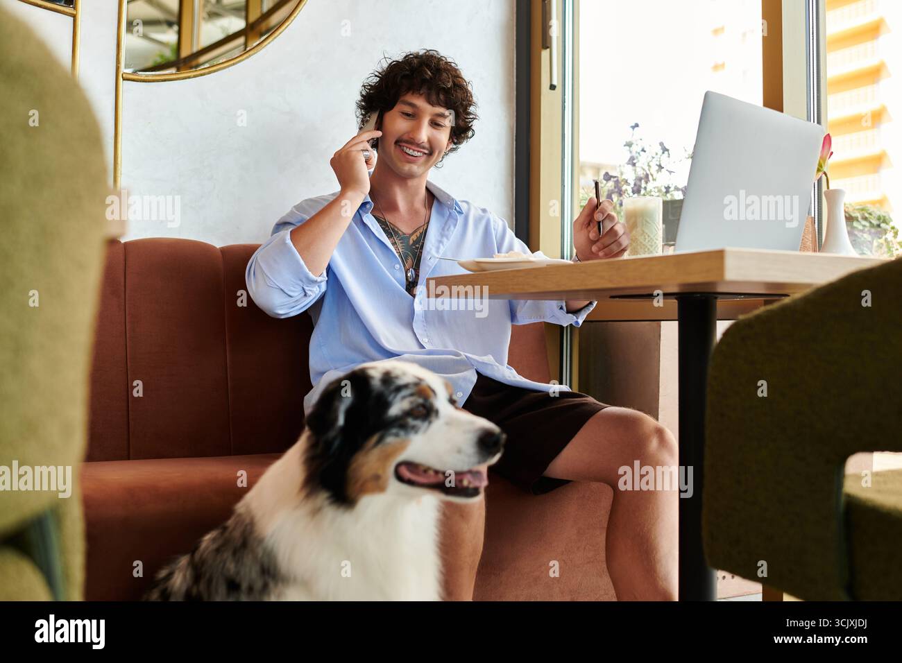 A young man smiles while speaking on the phone, seated comfortably in a ...