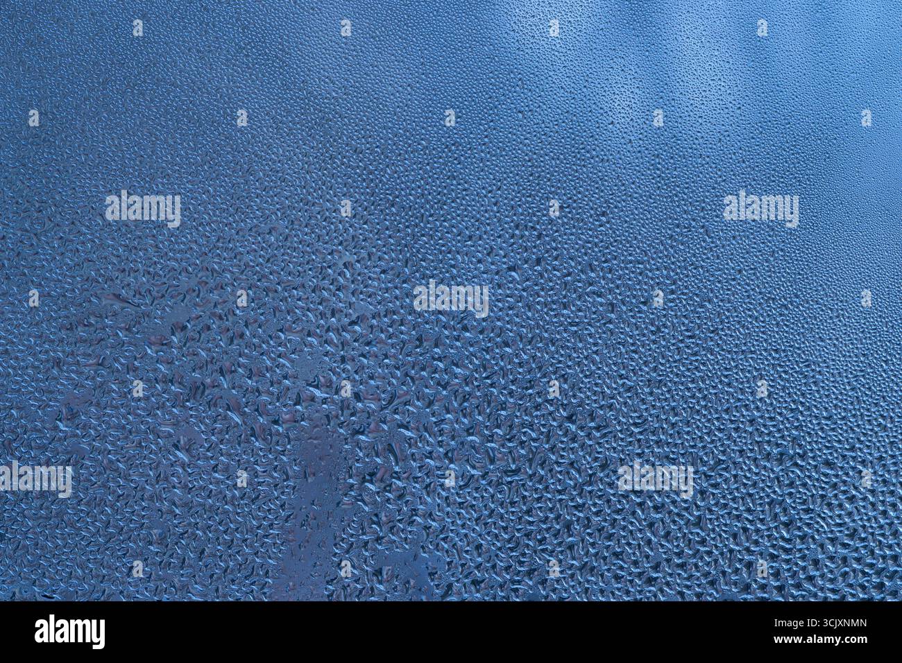 drops slowly sliding down wet window pane, creating winding paths on ...