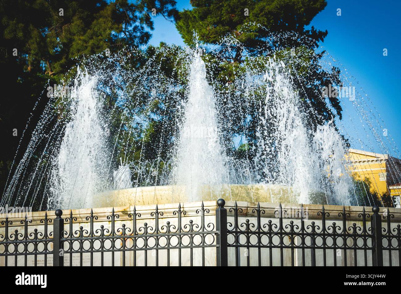 A marble fountain with strong water jets surrounded by an iron fence ...