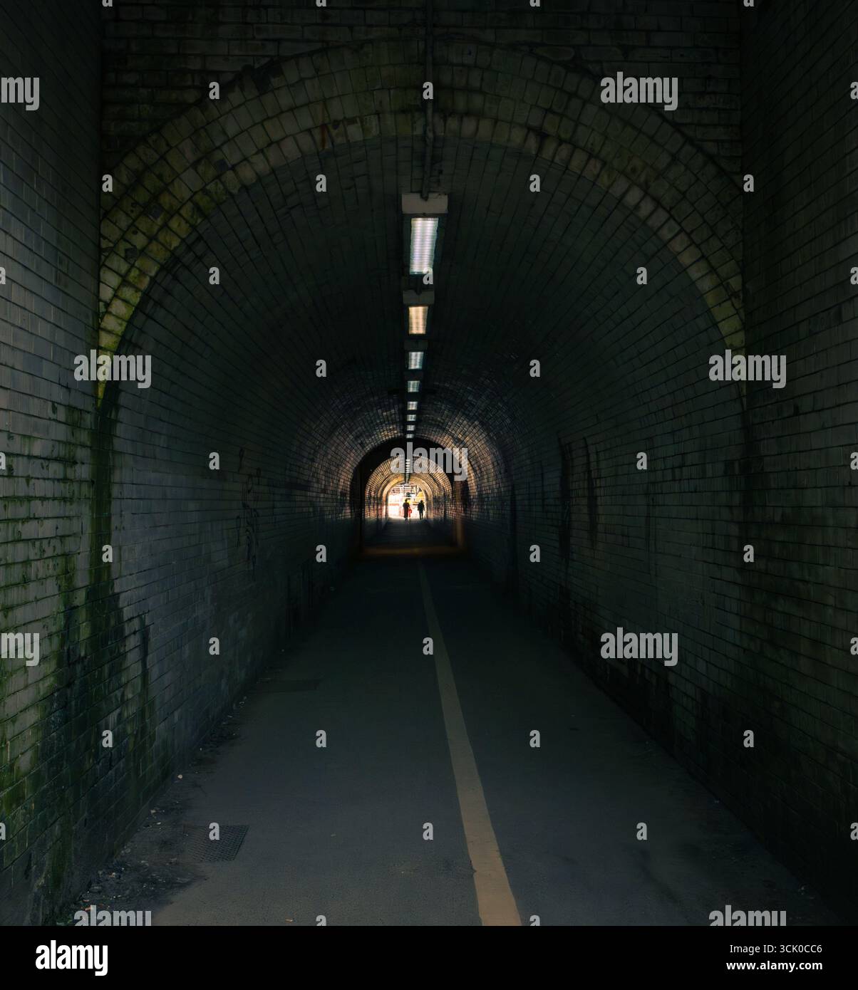 Dimly lit brick tunnel with yellow floor line, and silhouetted figures ...