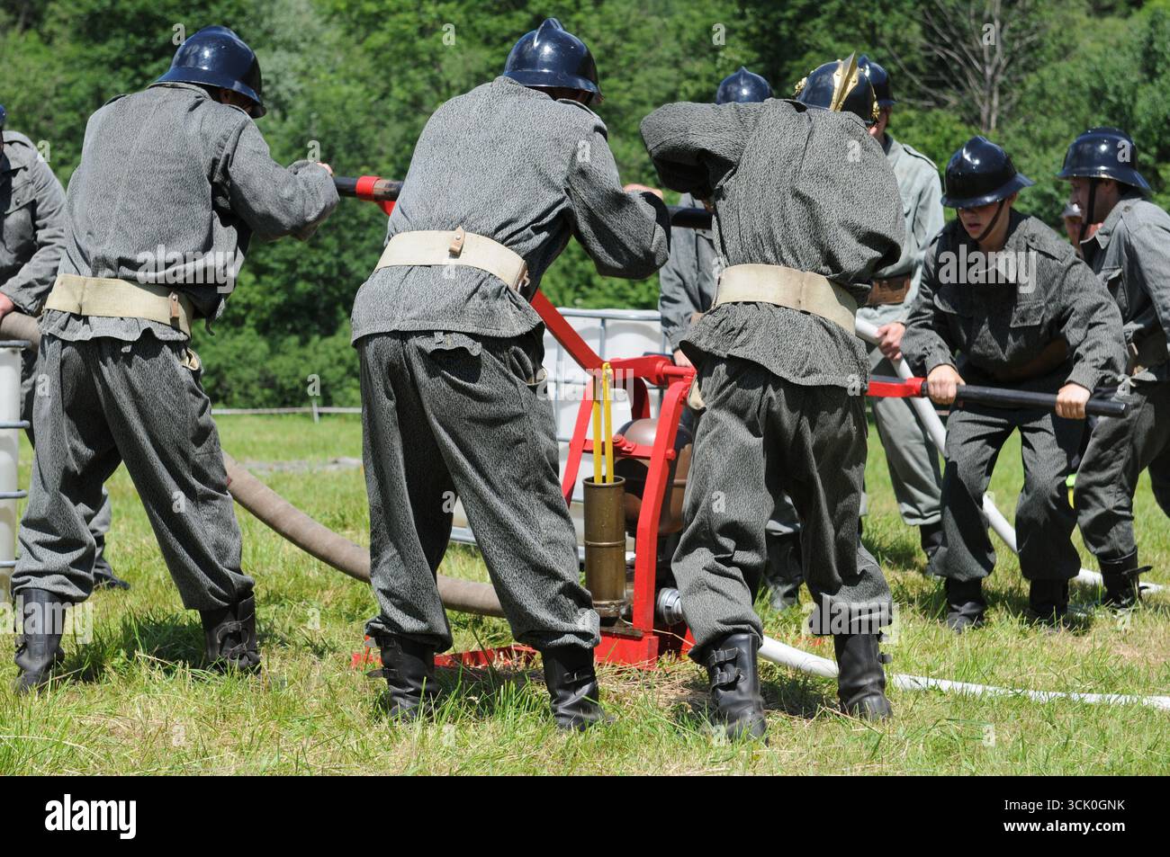 Firefighters in vintage uniforms operating a manual fire pump during a ...