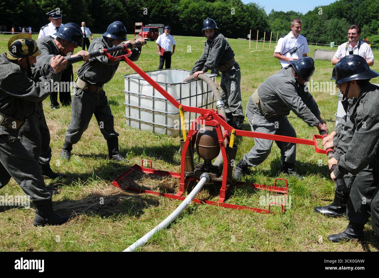 Firefighters in vintage uniforms operating a manual fire pump with ...