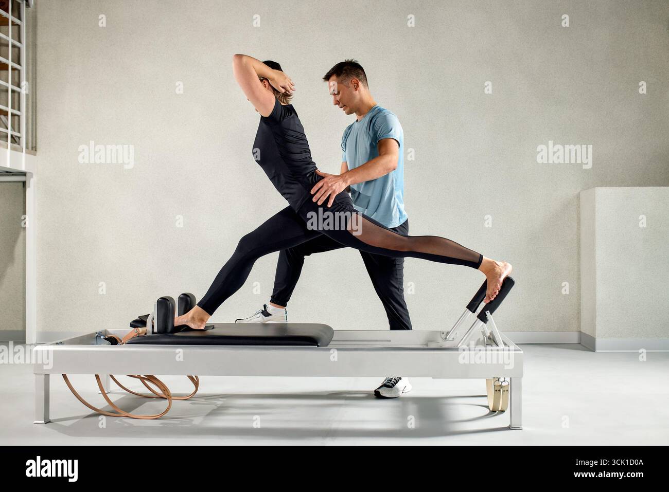 A fitness instructor supports a woman performing stretches on a Pilates ...
