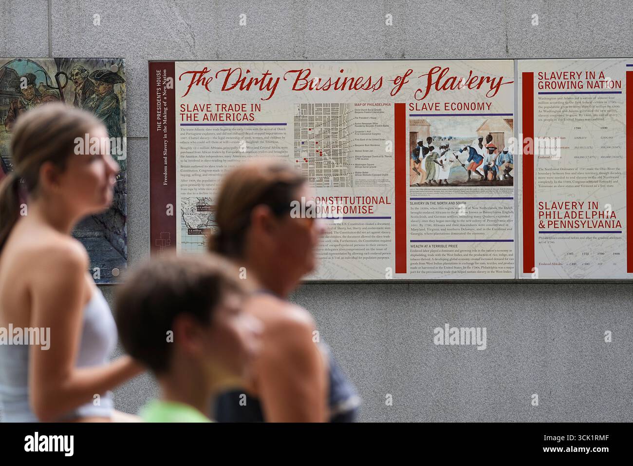 People walk past an informational panel at President's House Site ...