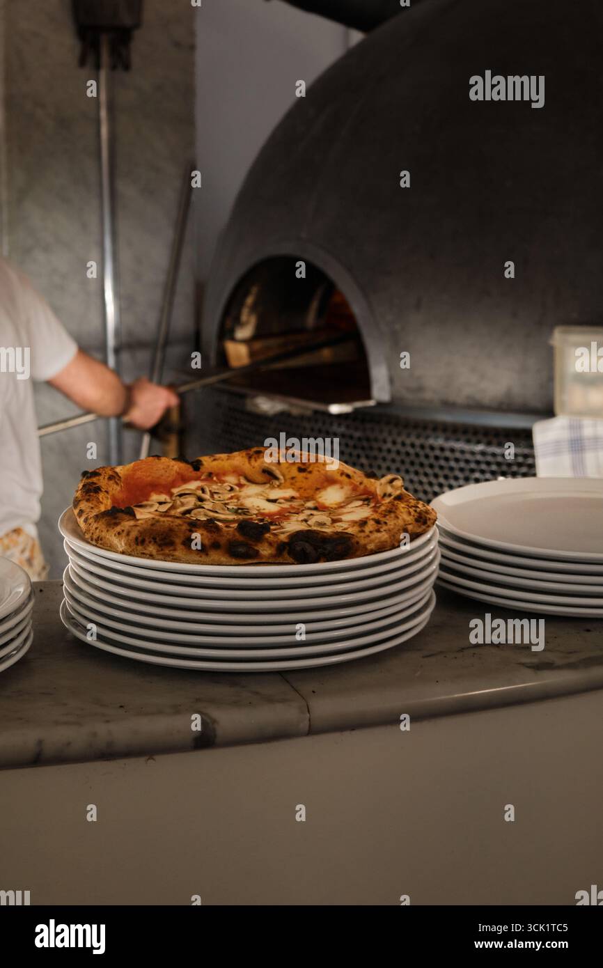 Freshly baked pizza resting on a stack of plates, with wood-fired oven ...