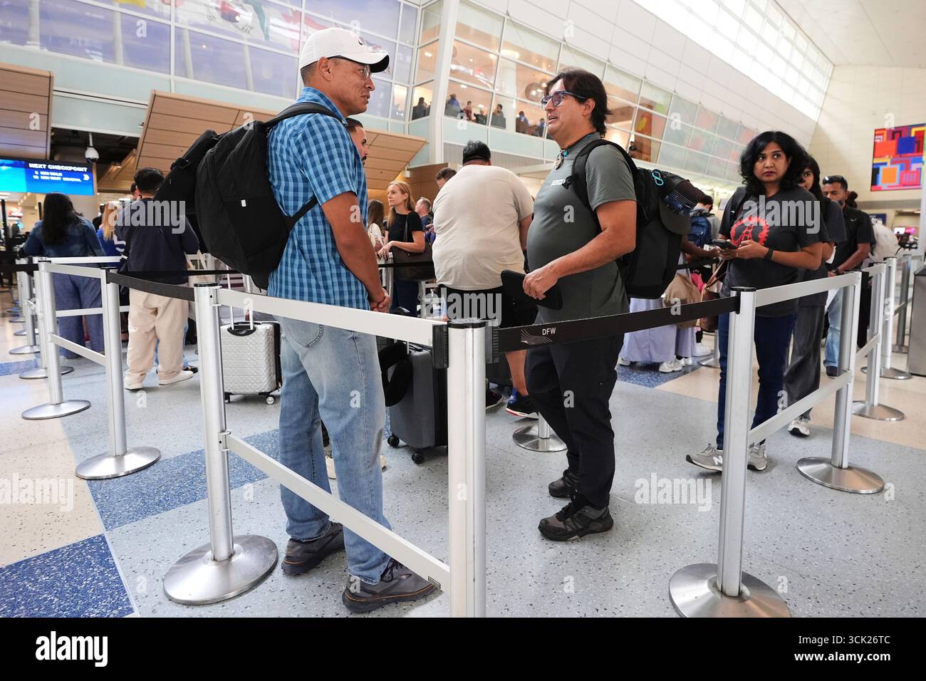 Travelers stand in line at a security checkpoint before boarding their ...