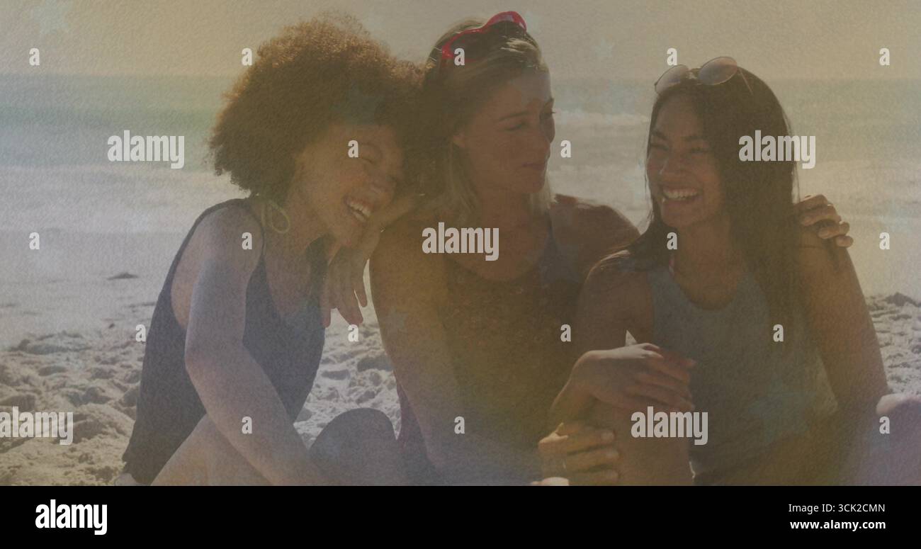 Smiling women leaning into each other on sandy ocean shoreline, with ...