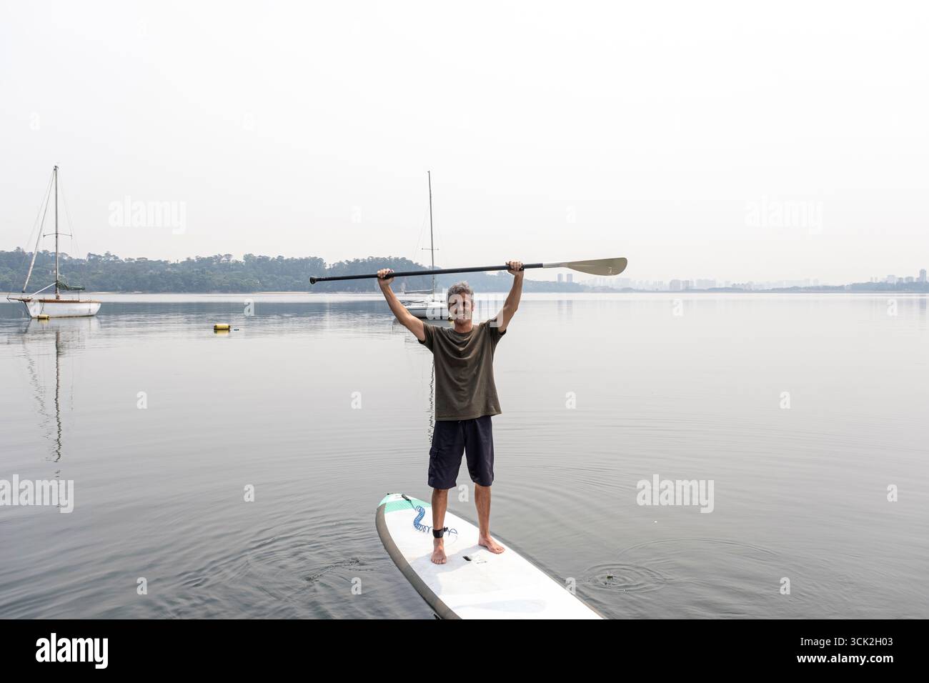 54 year old Brazilian on a standup paddleboard with the paddle over his ...