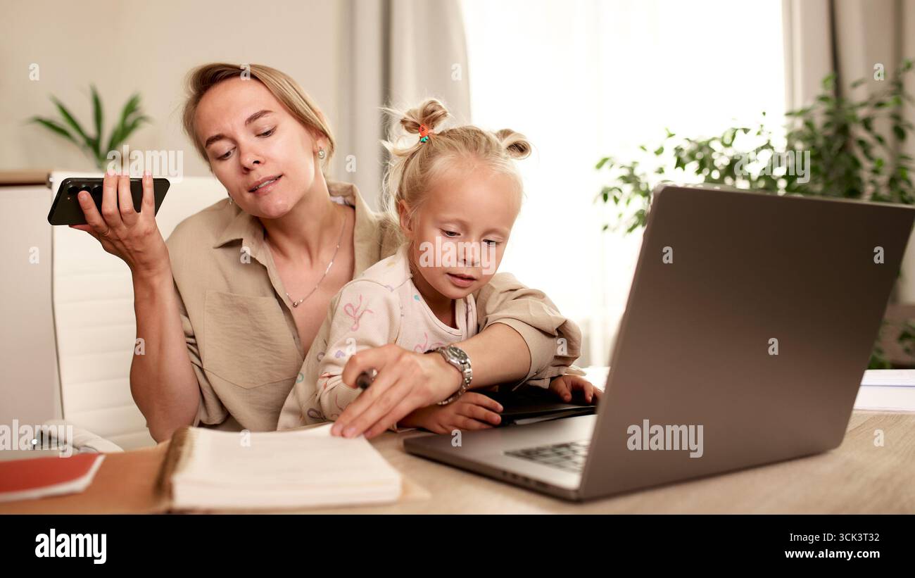 A mother is managing her work tasks while her daughter joins her at the ...