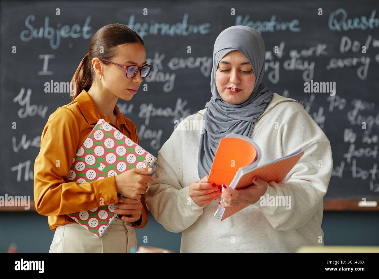 Female English Teacher and Middle Eastern Woman Reviewing Notebooks in ...