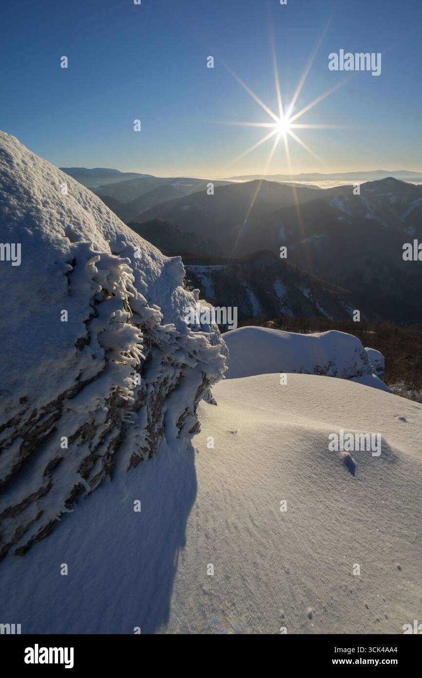 View of a sunburst over a snow-laden mountain peak, casting shadows on ...