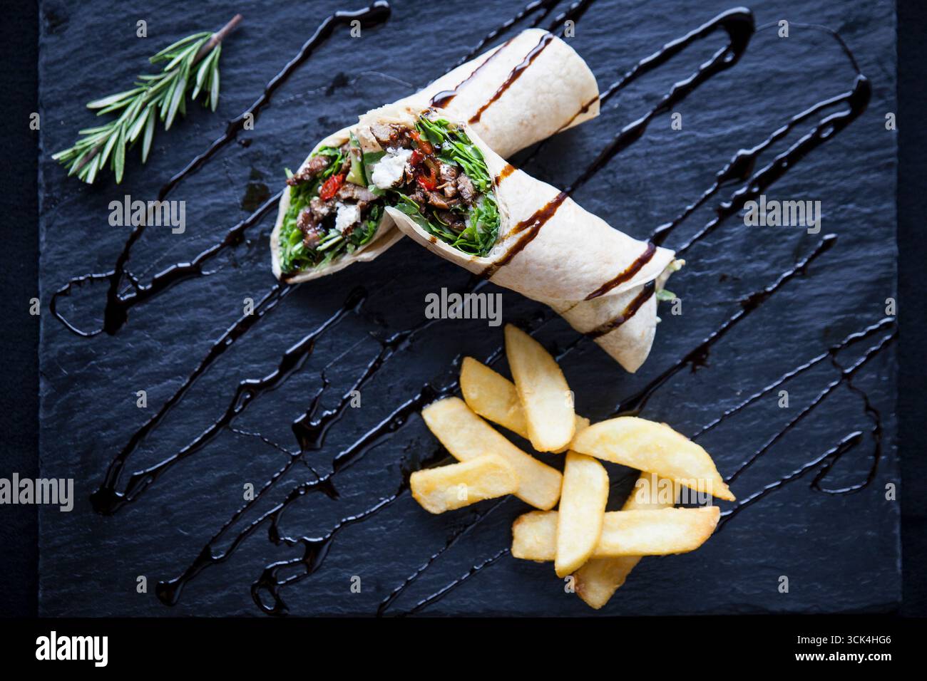 Overhead view of tortilla wraps with chips and sauce garnish on slate ...