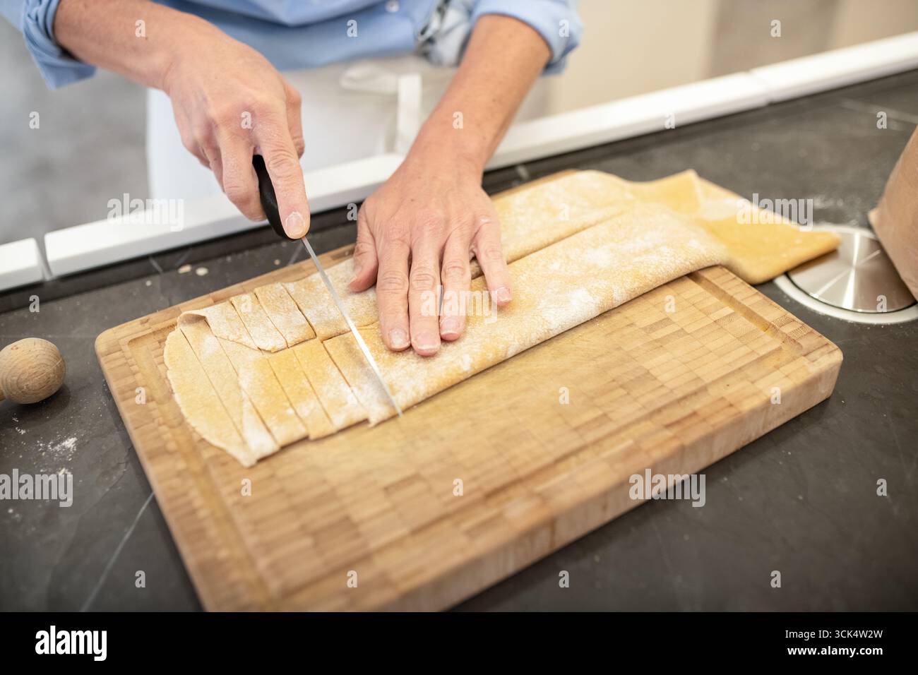 Woman cuts a dough into thin strips for the preparation of fresh pasta ...