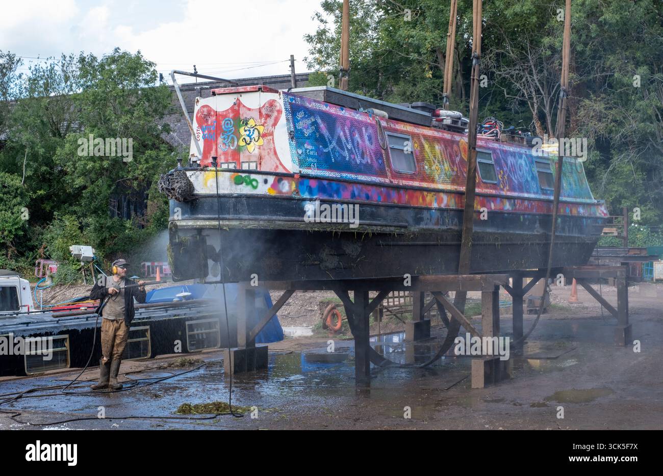 Brightly painted canal narrow boat hoisted by a crane and undergoing ...