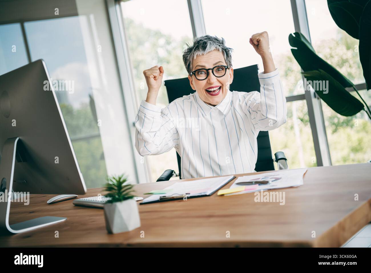 Excited businesswoman cheering at her office desk for success in ...