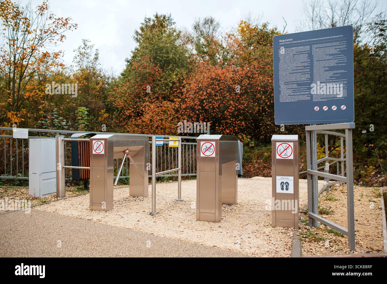 Outdoor turnstile entrance with informational sign and autumn foliage ...
