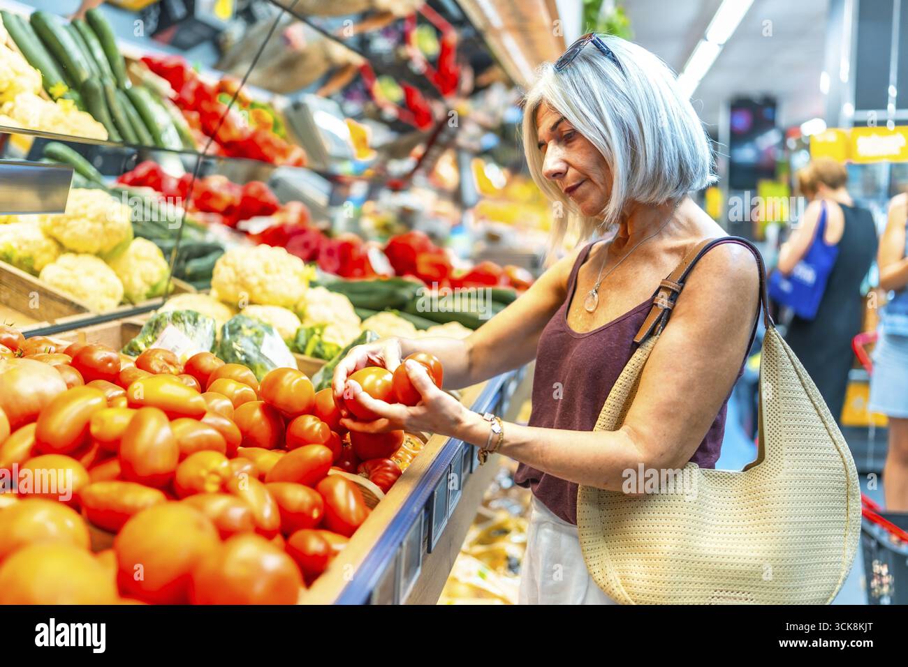 Senior woman carefully selecting fresh tomatoes from a vibrant display ...