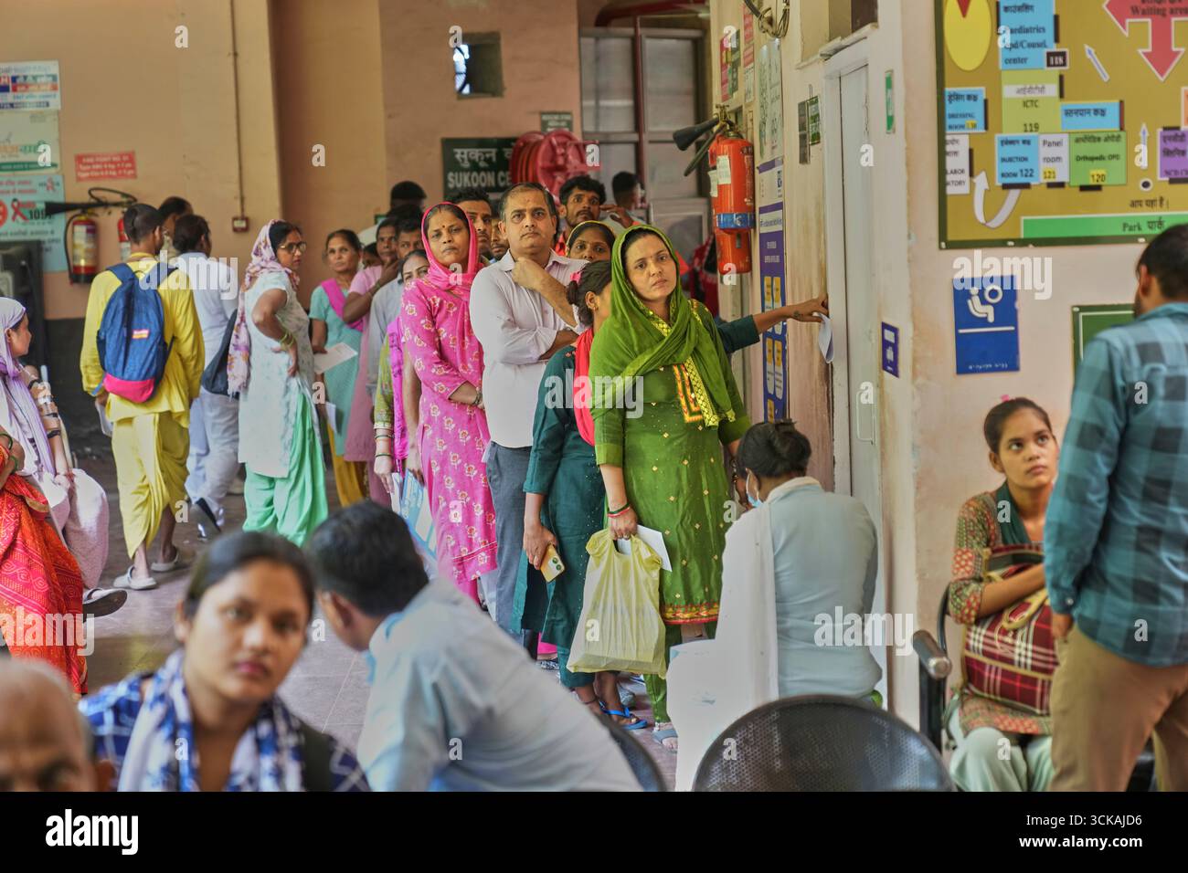 Patients stand in a queue outside a doctor's room while they watch a ...