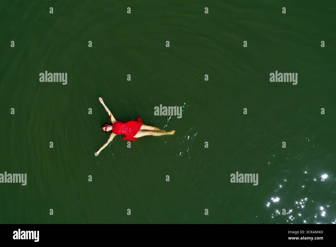 Aerial view of a woman in a red dress swimming in a calm, dark body of ...