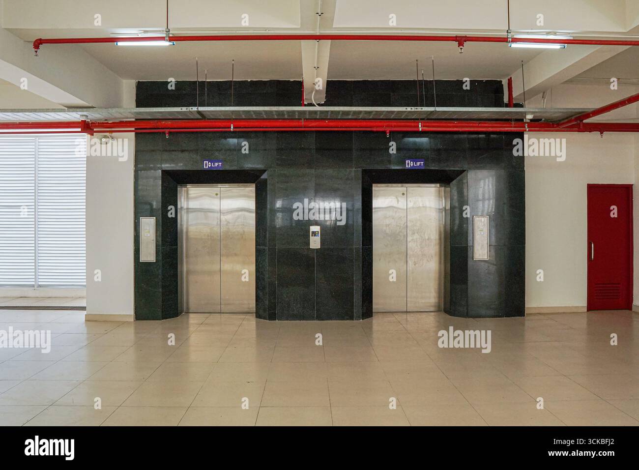 Two modern elevators in a commercial building lobby with red pipes ...