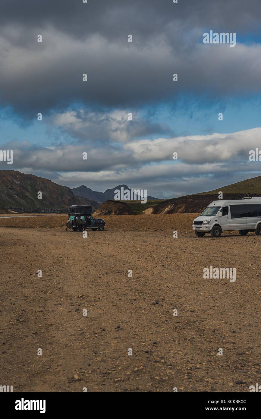 A white van and a roof rack equipped vehicle rest on barren ground with ...