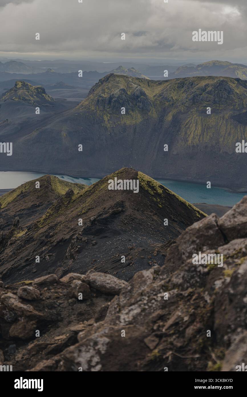 Rugged volcanic terrain with sharp ridges, a turquoise lake, and steep ...