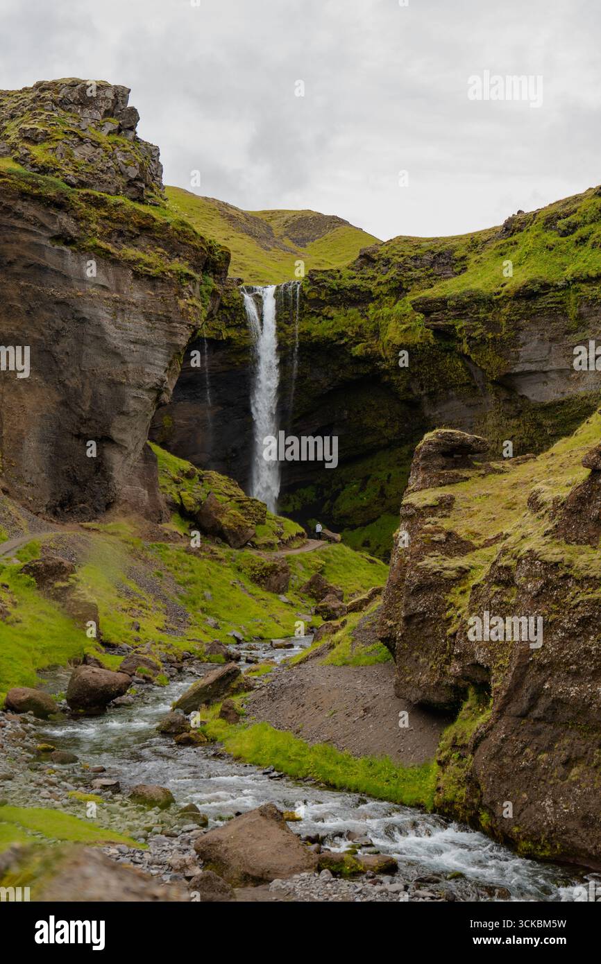 A waterfall flows from a rocky cliff into a narrow gorge, surrounded by ...