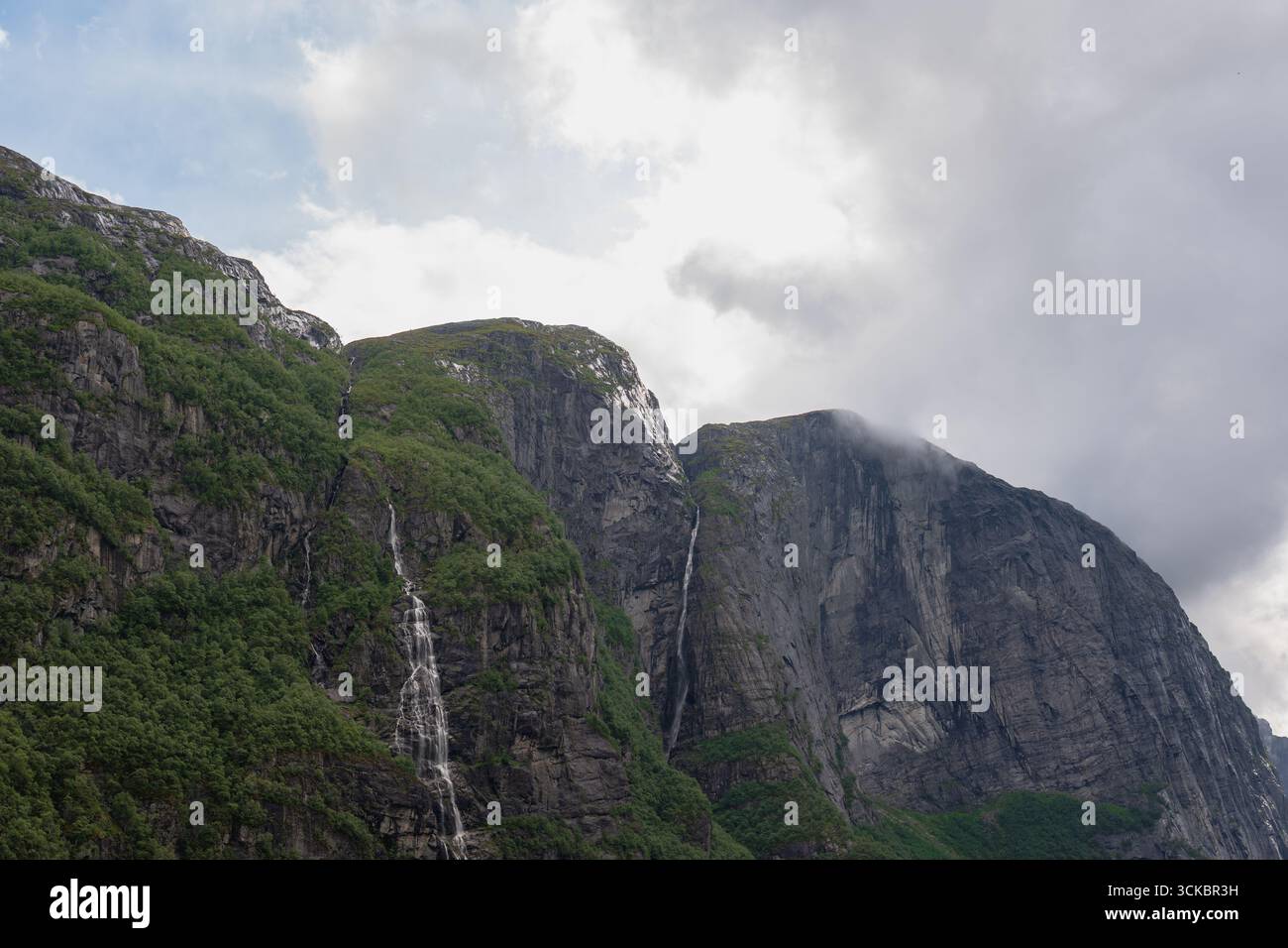 Steep cliffs with patches of greenery surround a cascading waterfall in ...