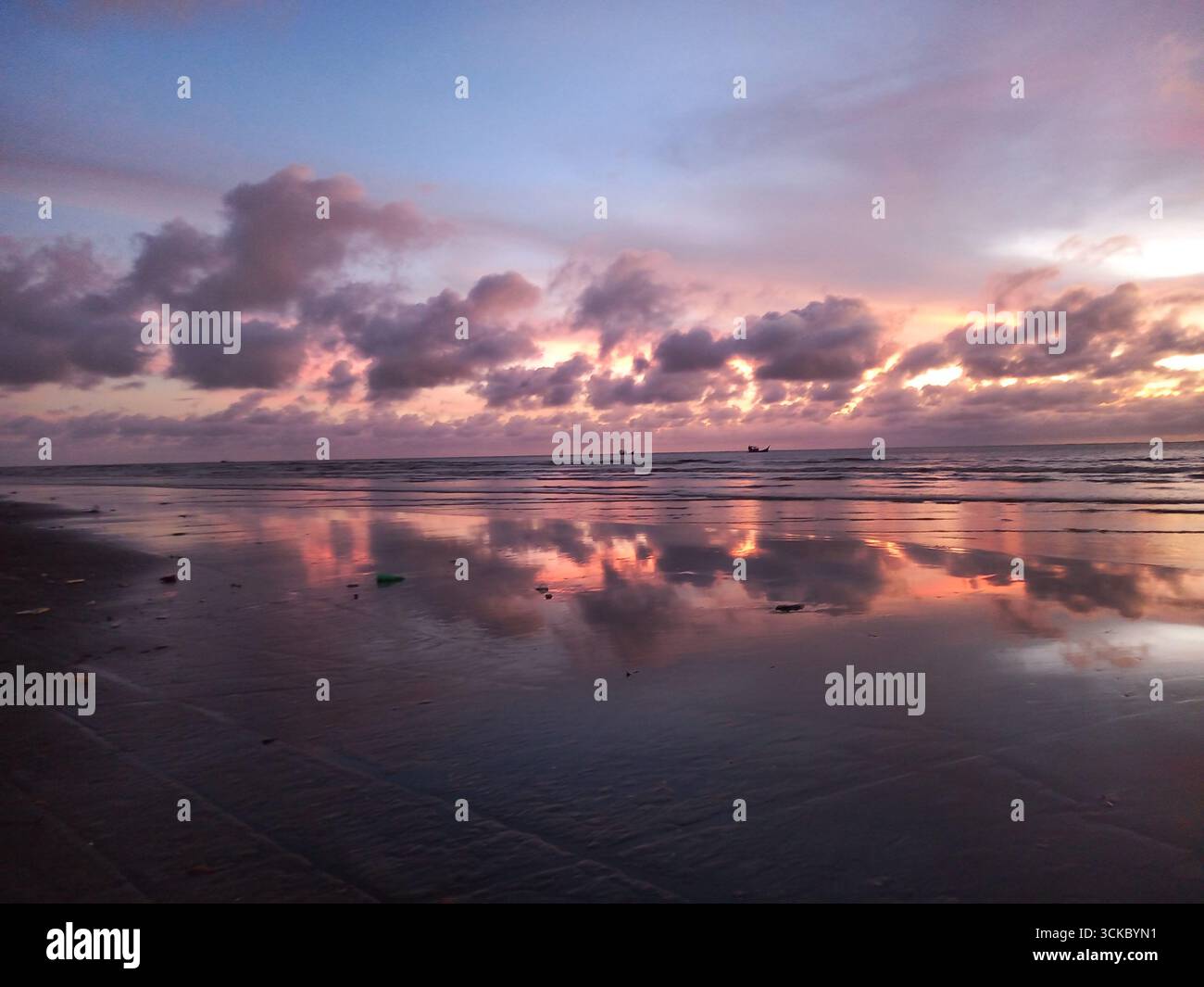 Breathtaking tropical sunset over a reflective wet beach with distant ...