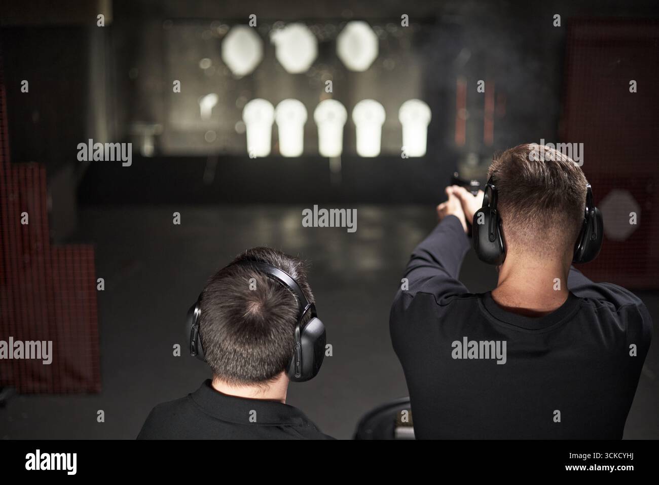 Two Caucasian men practicing shooting at indoor firing range, both ...